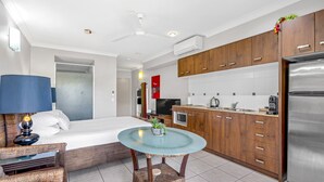 Quarto de hotel moderno com cama, mesa redonda pequena, sofá, televisão e cozinha compacta.