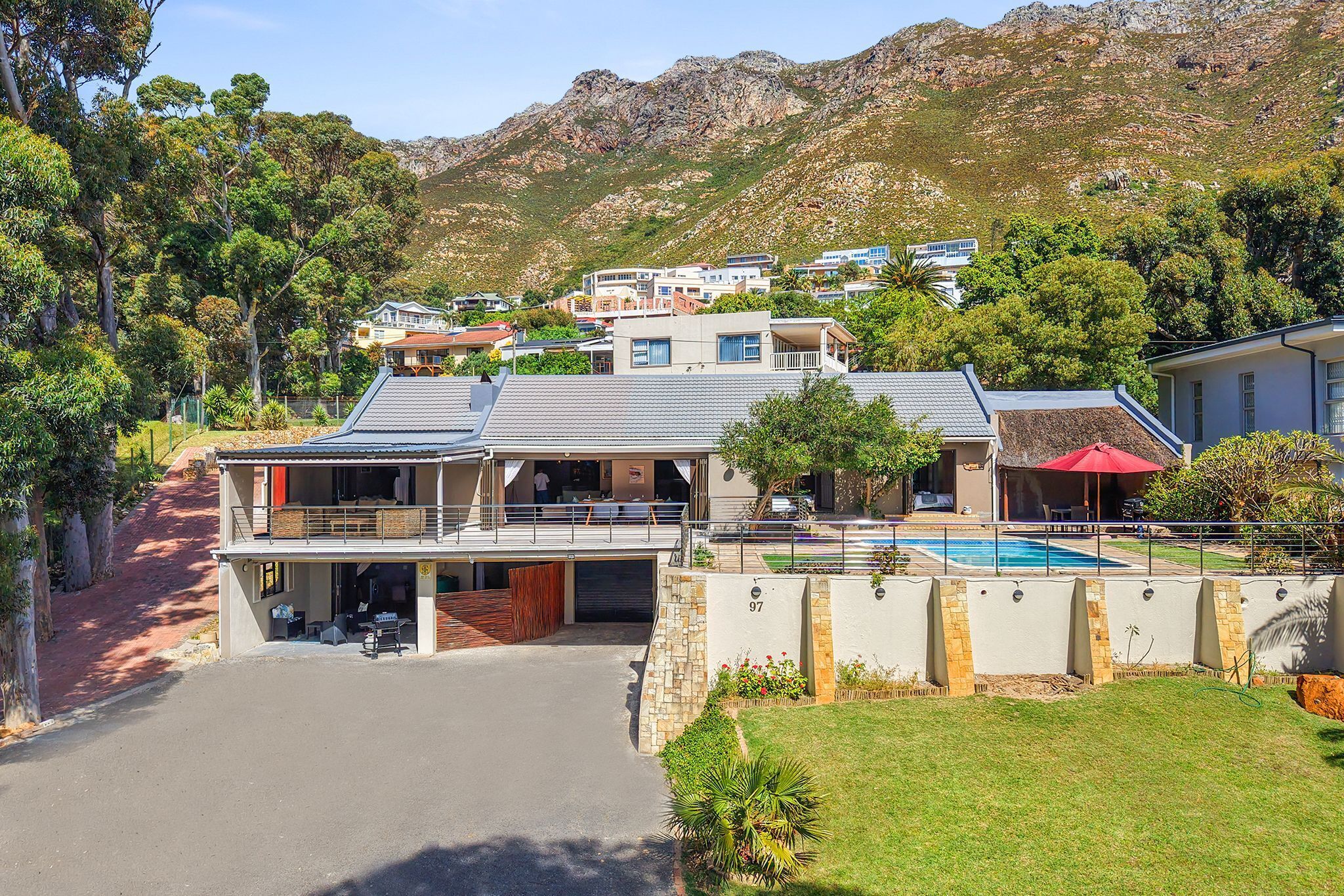 Uma casa moderna de dois andares com piscina, rodeada por vegetação exuberante e montanhas.