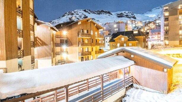Um edifício coberto de neve, com varandas de madeira e um teleférico ao fundo.