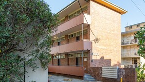 Um edifício de vários andares com fachada de tijolos, varandas e área de estacionamento.