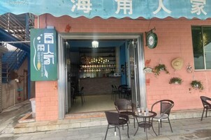 Fachada de loja com um letreiro que diz '海用人家' e uma placa verde com texto branco. Há áreas de estar ao ar livre com cadeiras e mesas.