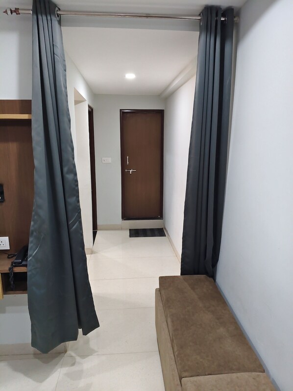 Quarto com um sofá marrom, uma estante de madeira, uma porta e uma tomada.