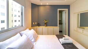 Quarto de hotel com cama, escrivaninha e janela com vista para um edifício.