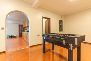 Uma mesa de futebolito em um quarto com piso de azulejos e uma porta que dá para outro cômodo com armários e espelho.