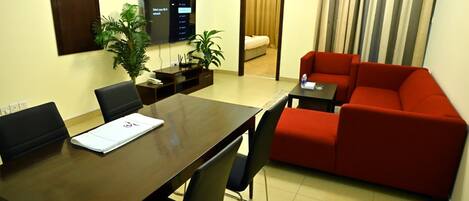 Quarto de hotel com mesa de jantar, sofá vermelho, televisão na parede e cama com cortinas.