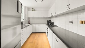 Uma cozinha moderna com armários brancos, piso de madeira e bancada preta.
