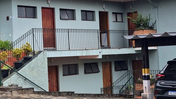 Um edifício de dois andares com uma varanda, uma antena parabólica e um carro estacionado em frente.