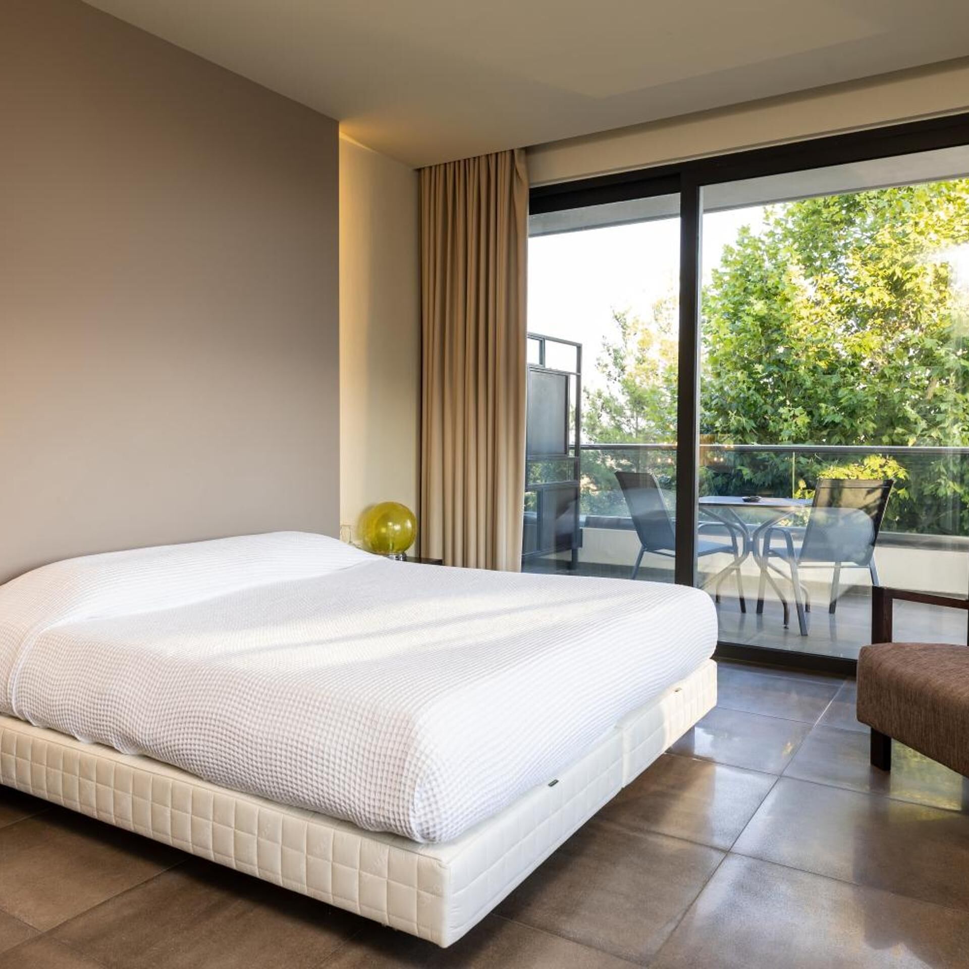 Quarto de hotel com uma cama grande, porta de vidro que dá para uma varanda e vista para árvores.
