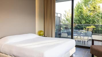 Quarto de hotel com uma cama grande, porta de vidro que dá para uma varanda e vista para árvores.