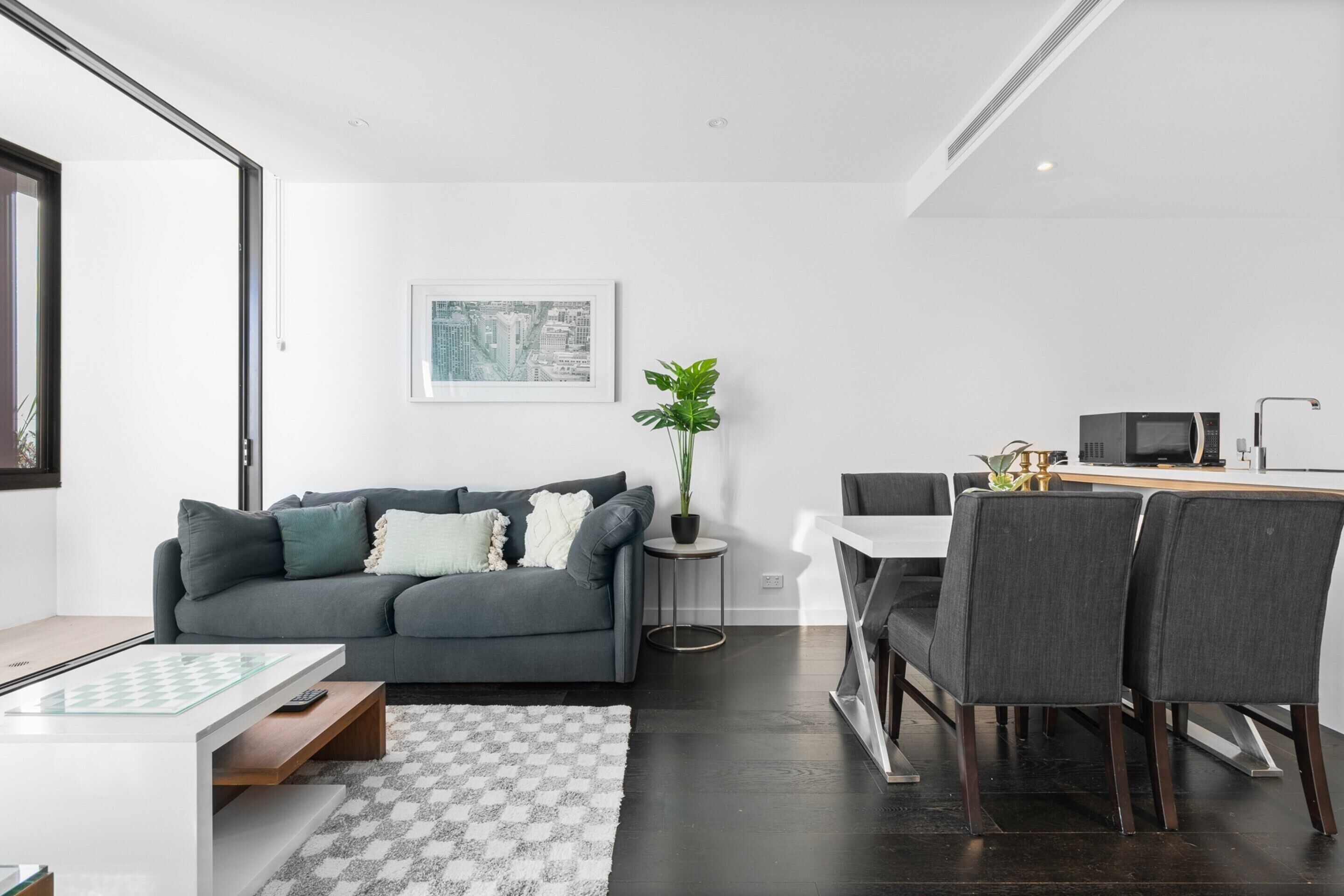 Uma sala de estar moderna com um sofá cinza, uma mesa de centro e uma área de jantar com uma mesa branca e cadeiras cinzas.