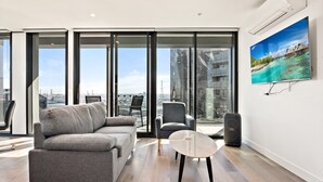 Uma sala de estar moderna com um sofá cinzento, uma mesa redonda pequena e uma janela grande com vista para a cidade.