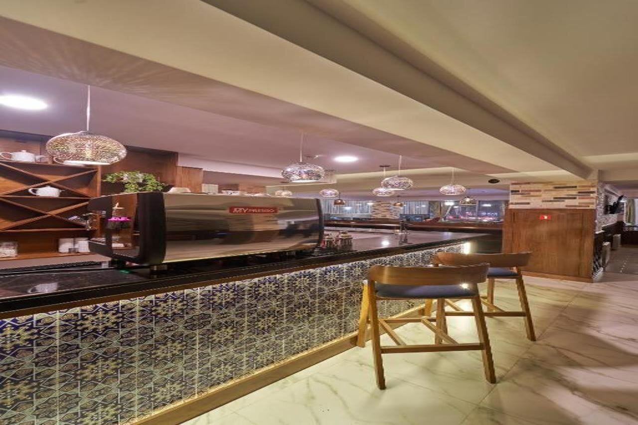 Uma área de bar moderna com máquina de café, banquetas e iluminação pendente.