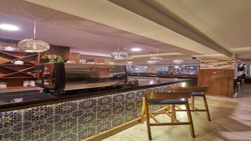 Uma área de bar moderna com máquina de café, banquetas e iluminação pendente.