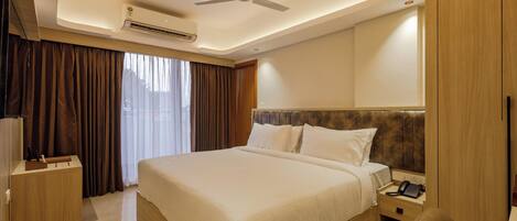 Quarto de hotel com uma cama grande, uma escrivaninha, uma cadeira, um guarda-roupa e um ventilador de teto.