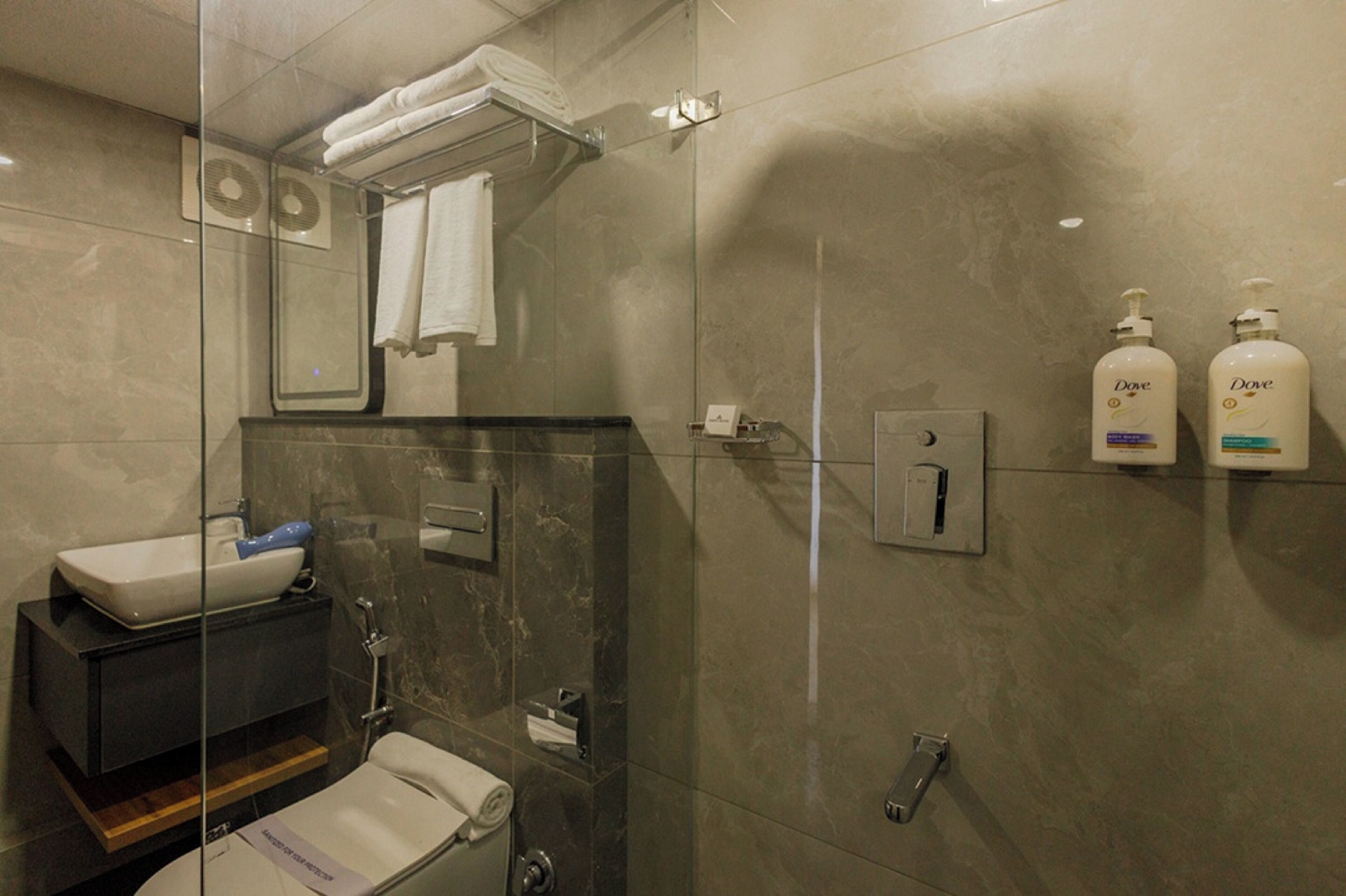 Um banheiro moderno com chuveiro em cabine de vidro, pia e duas embalagens de álcool em gel Dove em um dosador fixado na parede.