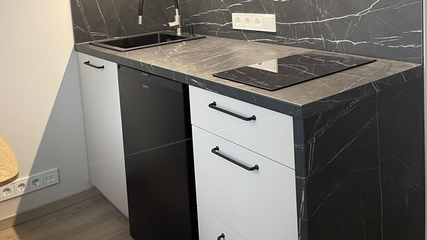 Uma cozinha moderna com bancada de mármore preto, pia embutida e armários brancos.