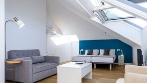 Um quarto moderno estilo loft com teto inclinado, um sofá cinzento, uma mesa de centro branca, uma cama com paredes azuis de destaque e um claraboia.