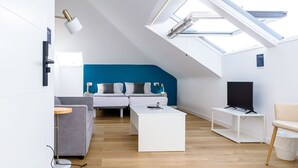 Um quarto moderno no estilo loft, com claraboia, cama, televisão e área de estar com sofá e poltrona.