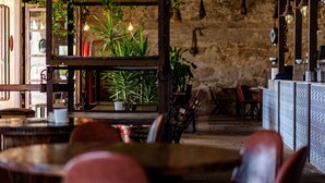 Restaurante com paredes de pedra rústicas, mobiliário de madeira e plantas em vasos.