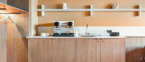 Uma cozinha moderna com armários de madeira, máquina de café expresso integrada e prateleiras brancas acima do balcão.