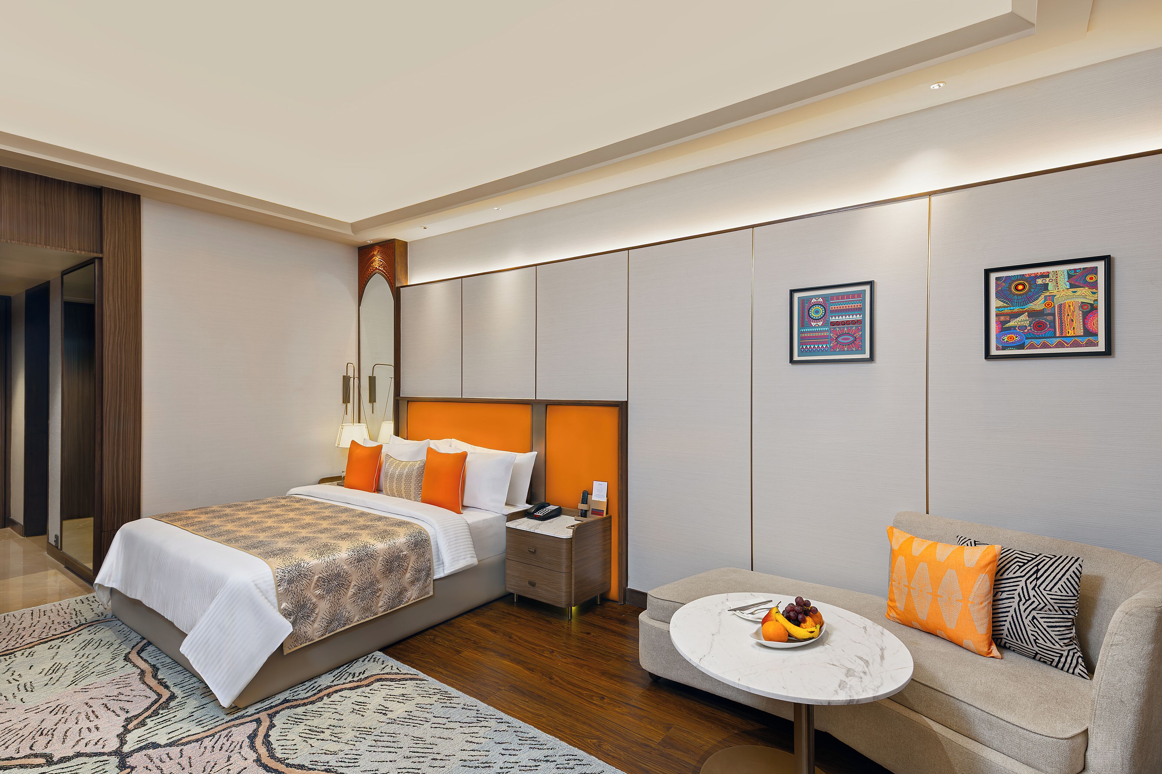 Quarto de hotel com cama, mesa de cabeceira, sofá e uma pequena mesa redonda com frutas.