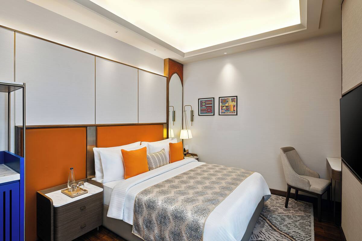 Quarto de hotel com cama, mesa de cabeceira, cadeira e um espelho grande.