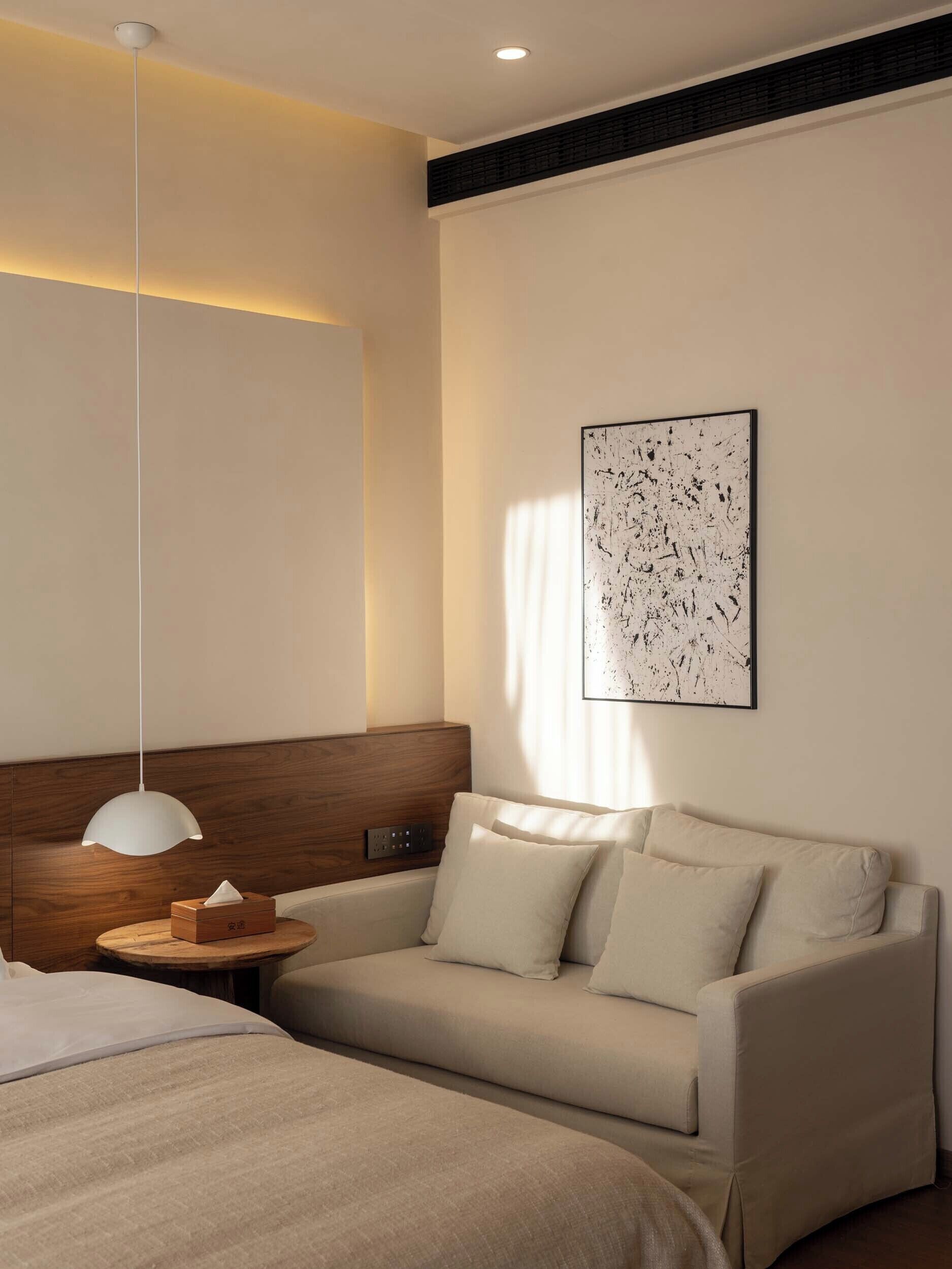 Quarto de hotel moderno com cama, sofá, mesa de cabeceira e obra de arte na parede.