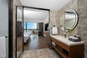 Quarto de hotel moderno com uma cama grande, banheiro com toucador e vista para a cidade.