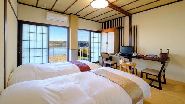 Quarto de hotel com duas camas, uma escrivaninha com televisão e janelas amplas com vista.