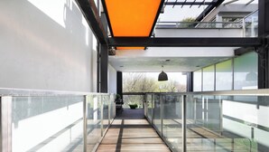 Corredor moderno com arquitetura marcante, guarda-corpos de vidro, soalho de madeira e vista para o exterior com vegetação.