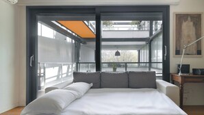 Quarto moderno com cama grande, porta de correr de vidro que dá para uma varanda e vista para a cidade.