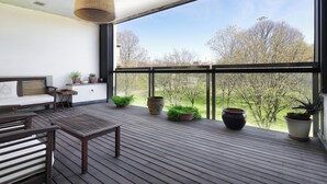 Varanda com piso de madeira, luminária pendente, sofá e vários vasos de plantas.