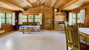 Uma cabana com interior de madeira, uma cama, uma mesa de jantar e um lustre.