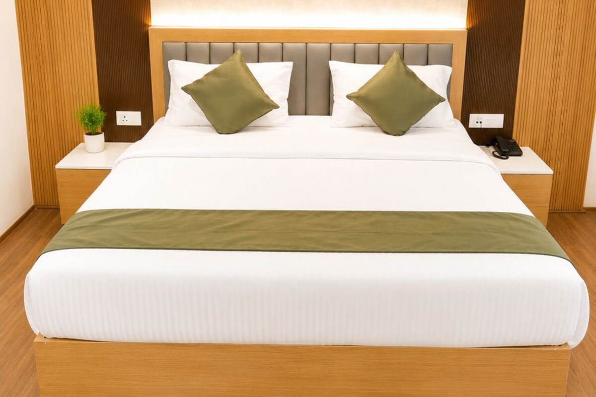 Quarto de hotel moderno com uma cama grande, mesa de cabeceira com telefone e uma pequena planta.