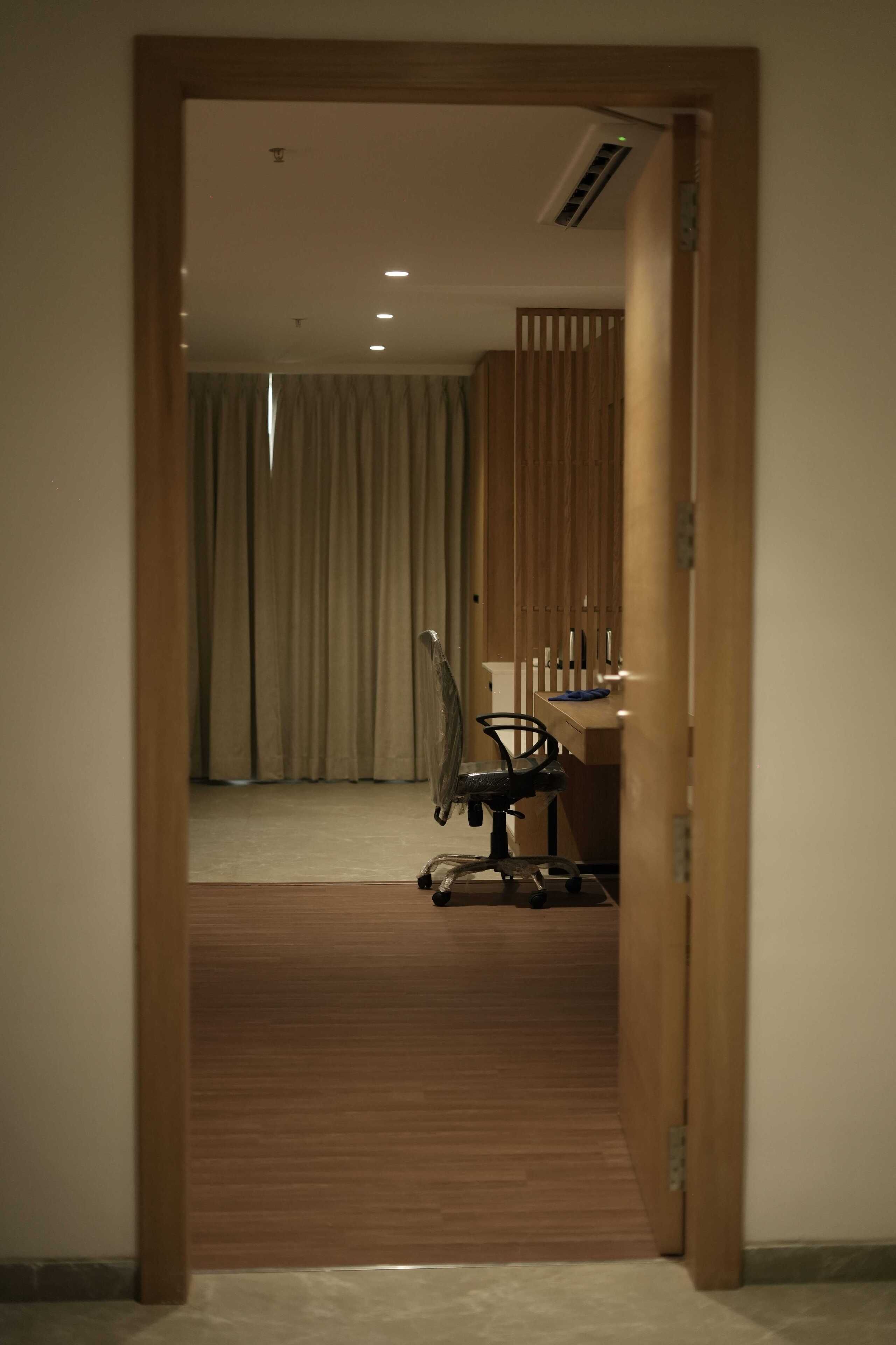 Quarto de hotel com piso de madeira, uma escrivaninha com cadeira e uma cortina ao fundo.