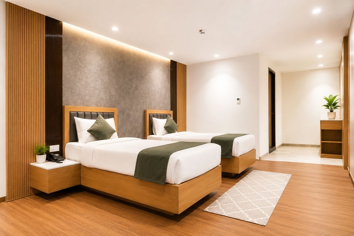 Quarto de hotel moderno com duas camas, cabeceiras de madeira, uma mesinha de cabeceira com telefone, uma pequena planta e um tapete em tons neutros.