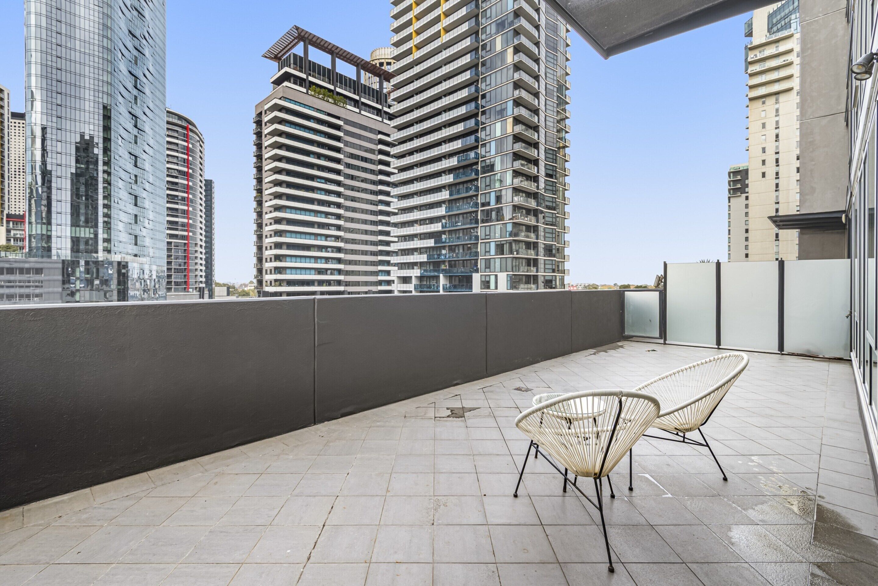 Terraço no telhado com duas cadeiras de vime e vista para edifícios altos modernos.