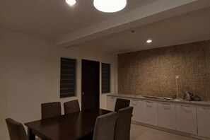 Uma área de refeições com uma mesa grande e cadeiras, uma cozinha com revestimento de parede estampado e um teto com iluminação embutida.