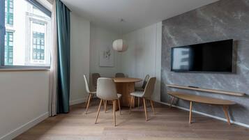 Uma sala de jantar moderna com uma mesa redonda, seis cadeiras, um banco e uma televisão fixada em uma parede de mármore.