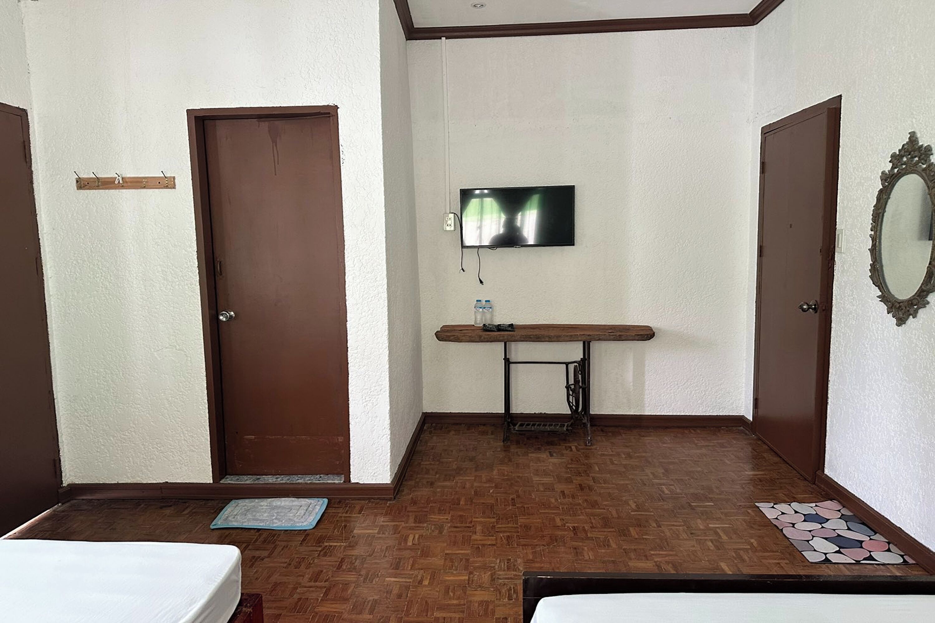 Quarto de hotel com chão de madeira, uma cama, uma escrivaninha com cadeira, televisão na parede e uma porta.