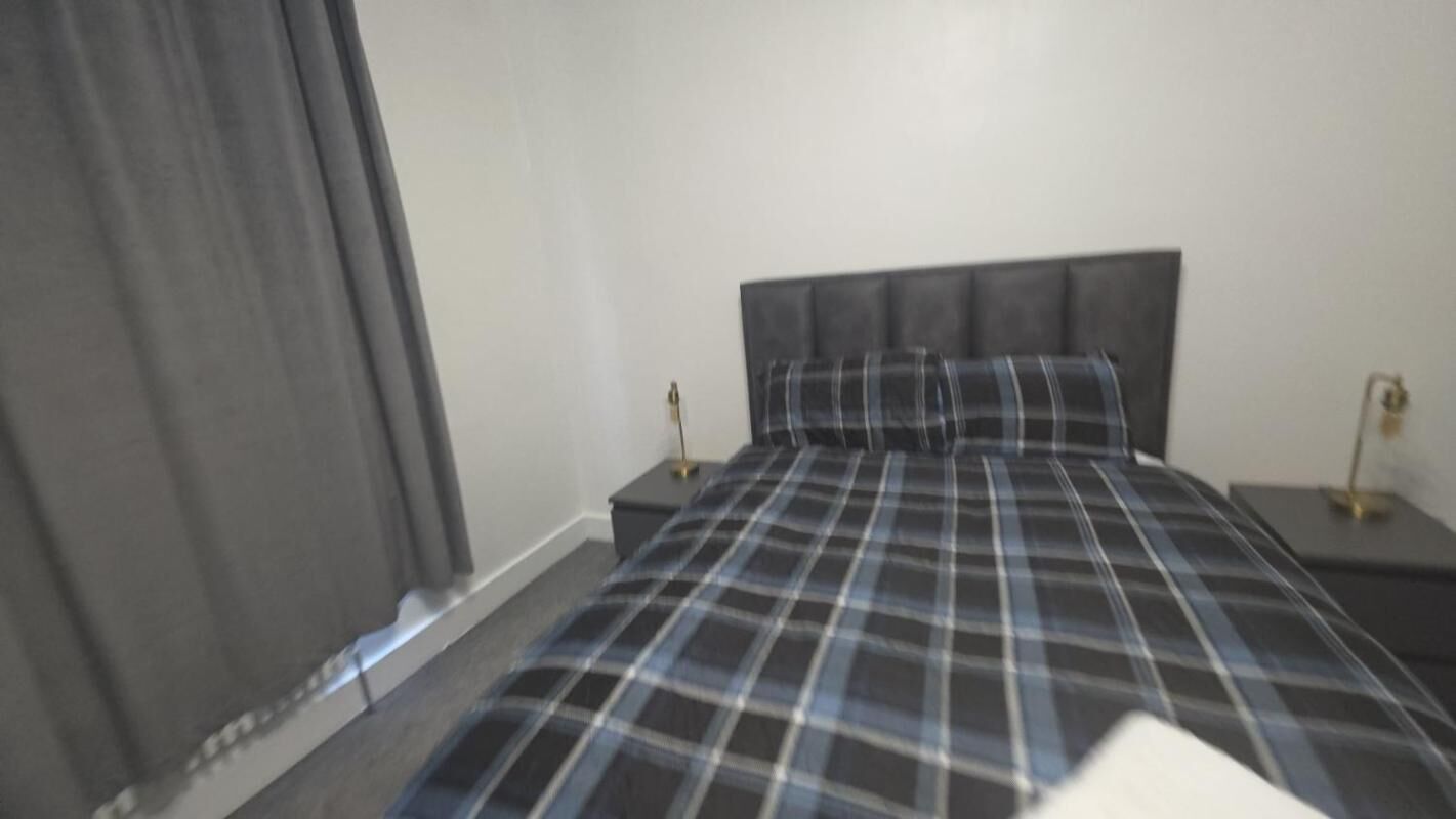 Quarto com cama, mesa de cabeceira, abajur e cortina.