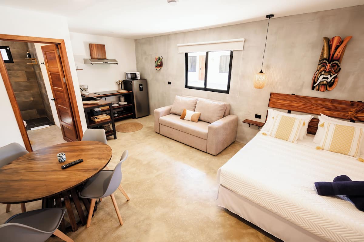 Quarto de hotel compacto com cama, sofá, mesa de jantar e cozinha compacta.