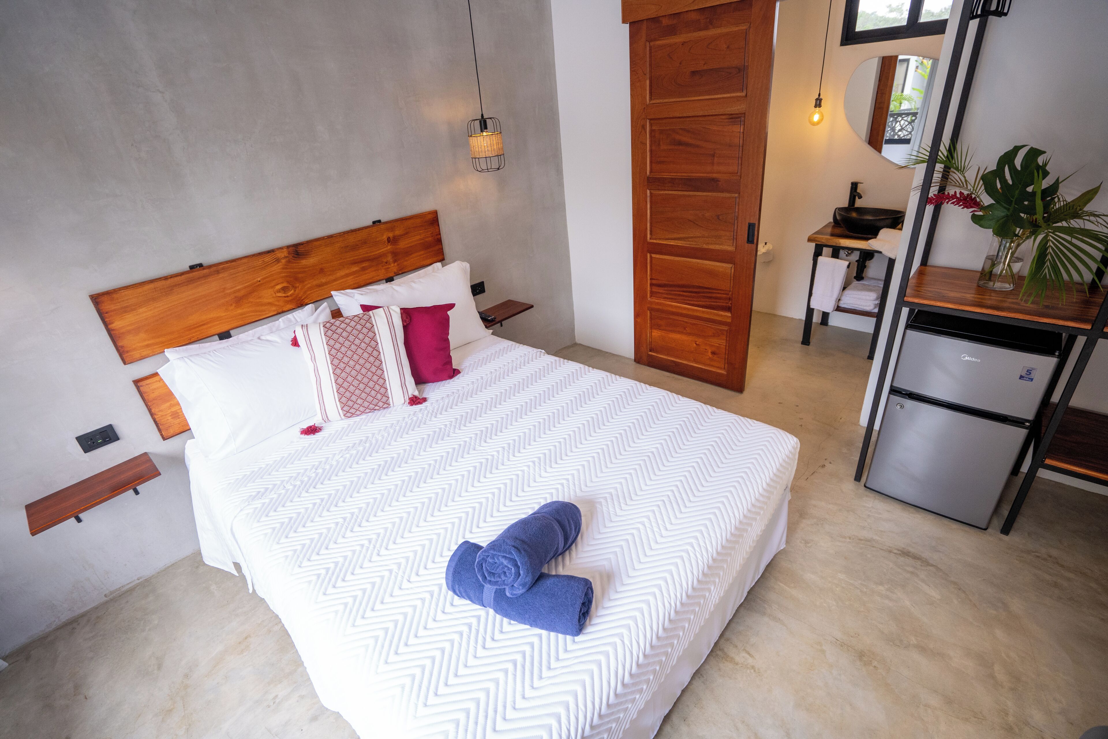 Cama bem arrumada com cabeceira de madeira, mesa de cabeceira pequena com pia e espelho.