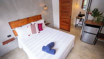 Cama bem arrumada com cabeceira de madeira, mesa de cabeceira pequena com pia e espelho.