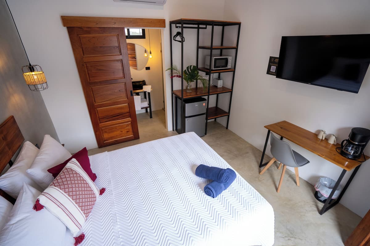 Quarto de hotel com cama, escrivaninha, televisão e guarda-roupa de madeira.