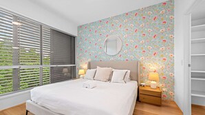Quarto com uma cama grande, mesa de cabeceira com abajur, espelho e papel de parede floral.