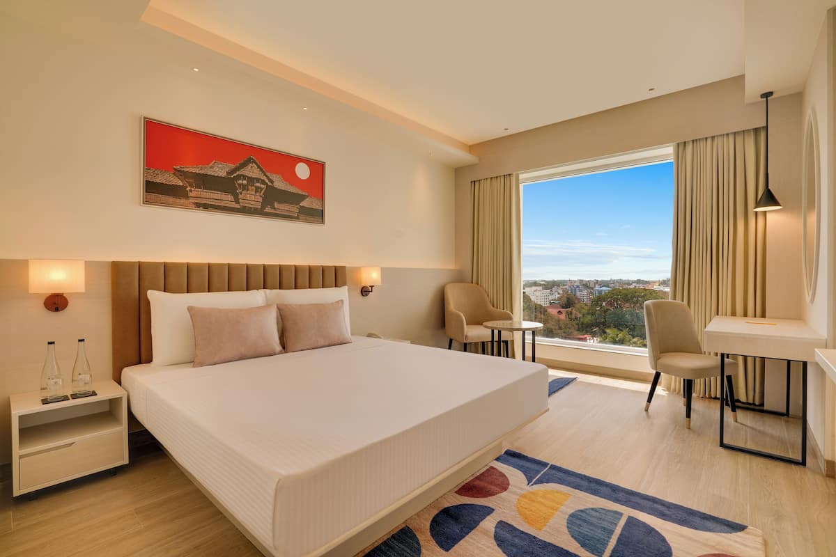 Quarto de hotel com uma cama grande, uma escrivaninha, uma cadeira, uma mesinha de cabeceira e vista para a cidade.