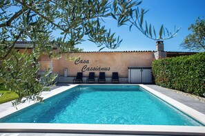 Uma piscina com espreguiçadeiras, uma parede com o texto 'Casa Cassianos' e um céu azul e límpido.