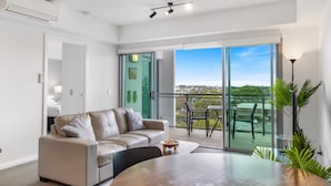 Uma sala de estar moderna com um sofá bege, uma mesa de madeira redonda e uma varanda com vista para a cidade.