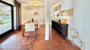 Uma sala de jantar com mesa de madeira e cadeiras brancas, um aparador preto com luminárias e obras de arte na parede.